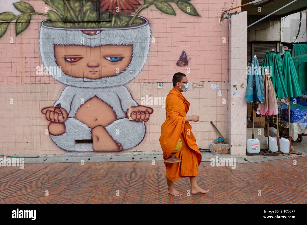 A Buddhist monk walks past a mural depicting a cartoonish character ...