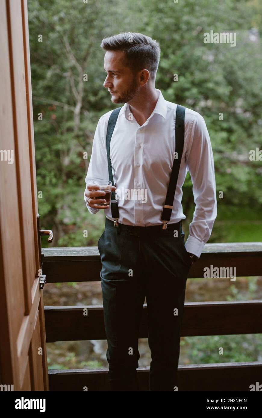 Elegantly dressed groom in a suit sitting on the balcony of a log ...