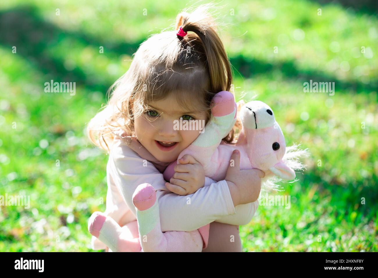 Happy baby girl hug toy having fun at the park. Funny baby child. Baby ...