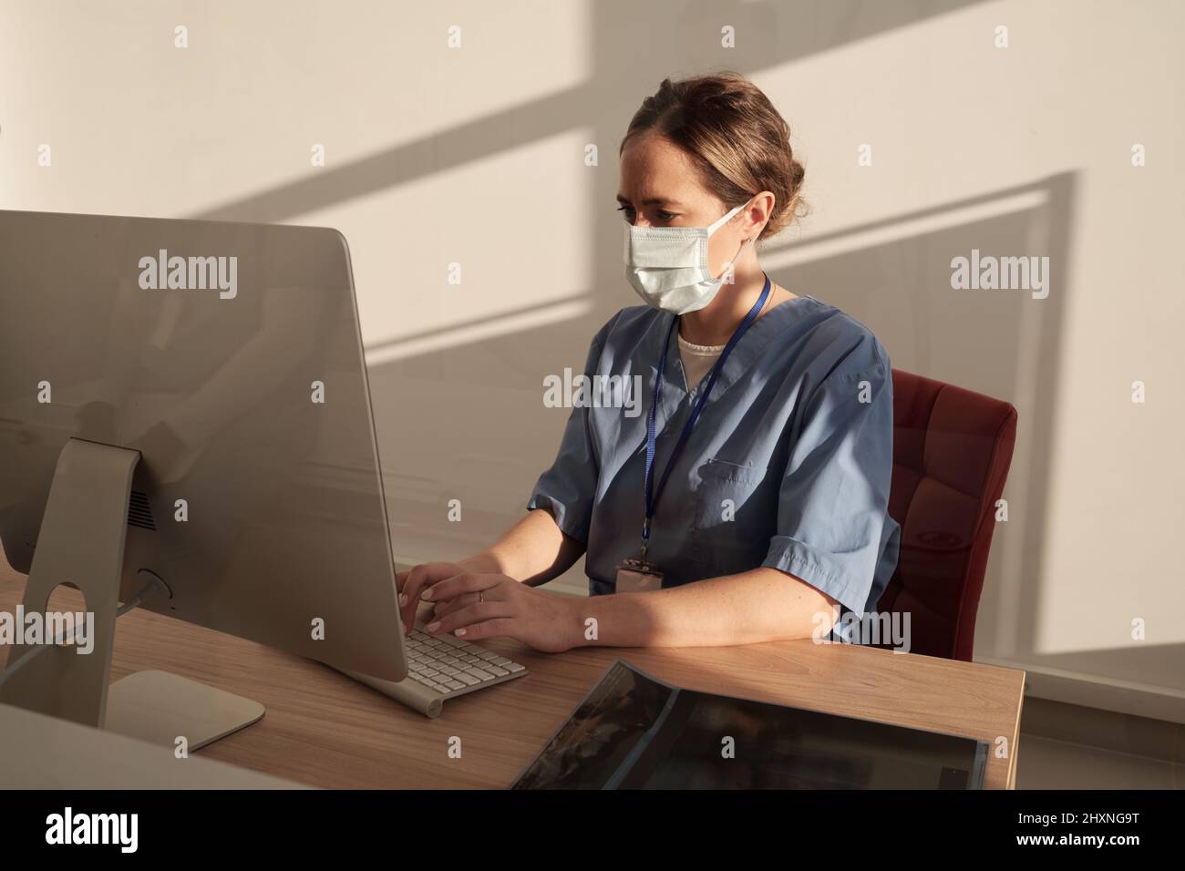 Young serious female clinician in mask and uniform entering medical ...
