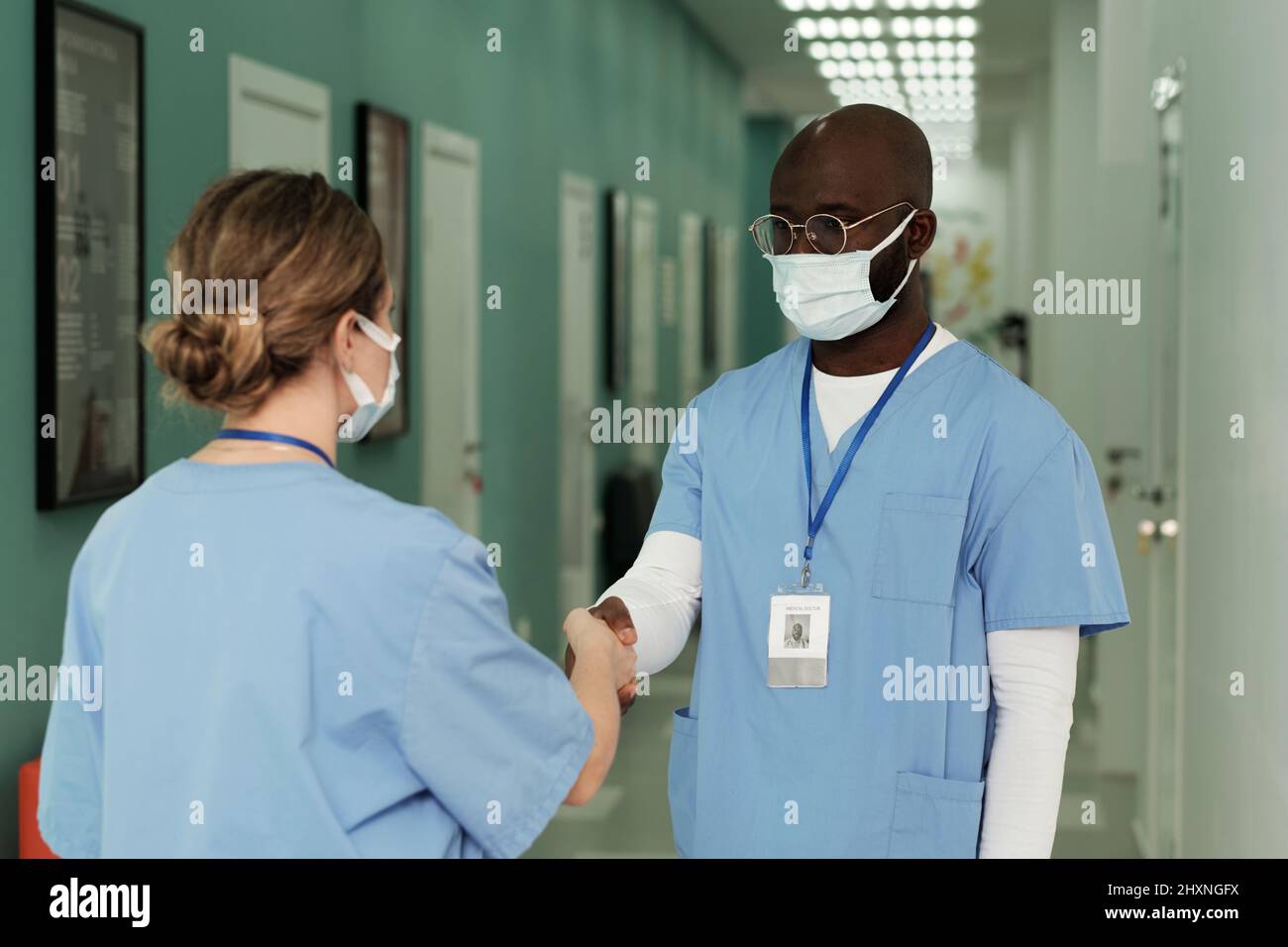 Young African American surgeon in uniform and protective mask shaking ...