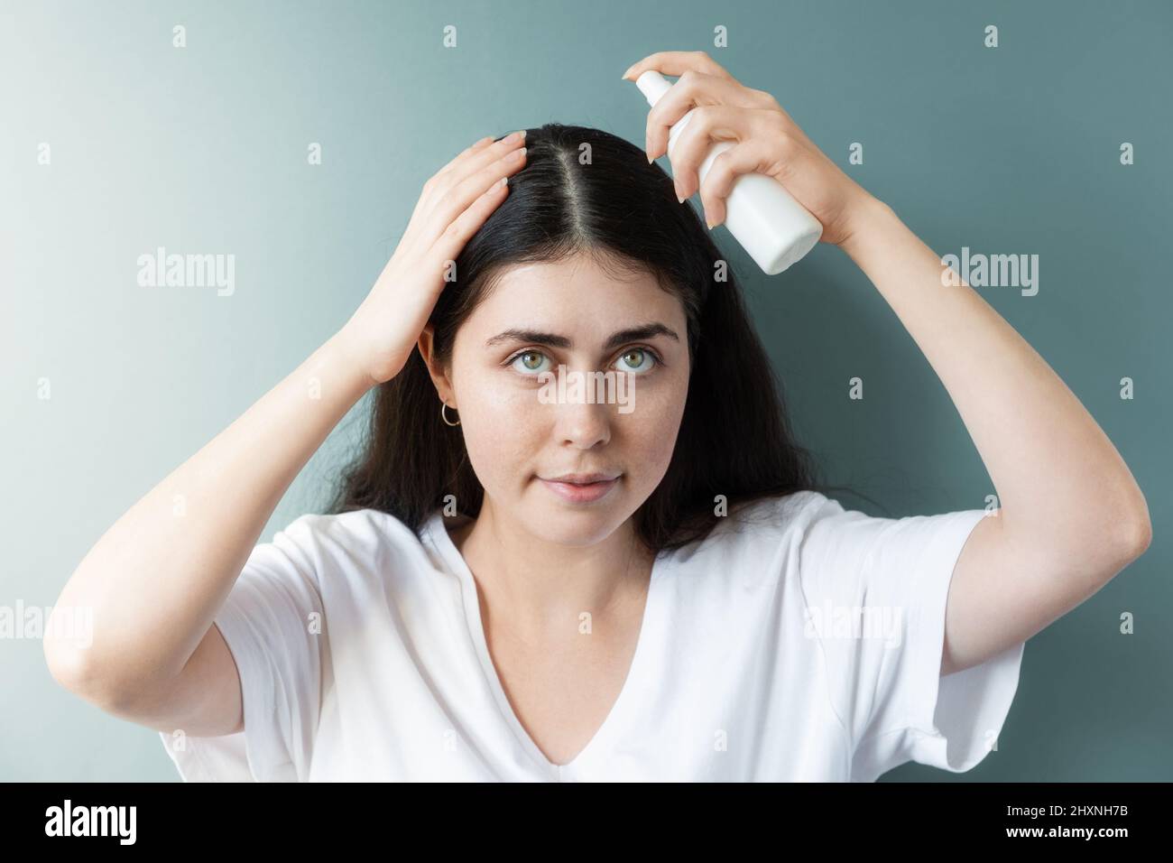 Portrait of a caucasian woman with dark hair applying spraying cosmetic ...