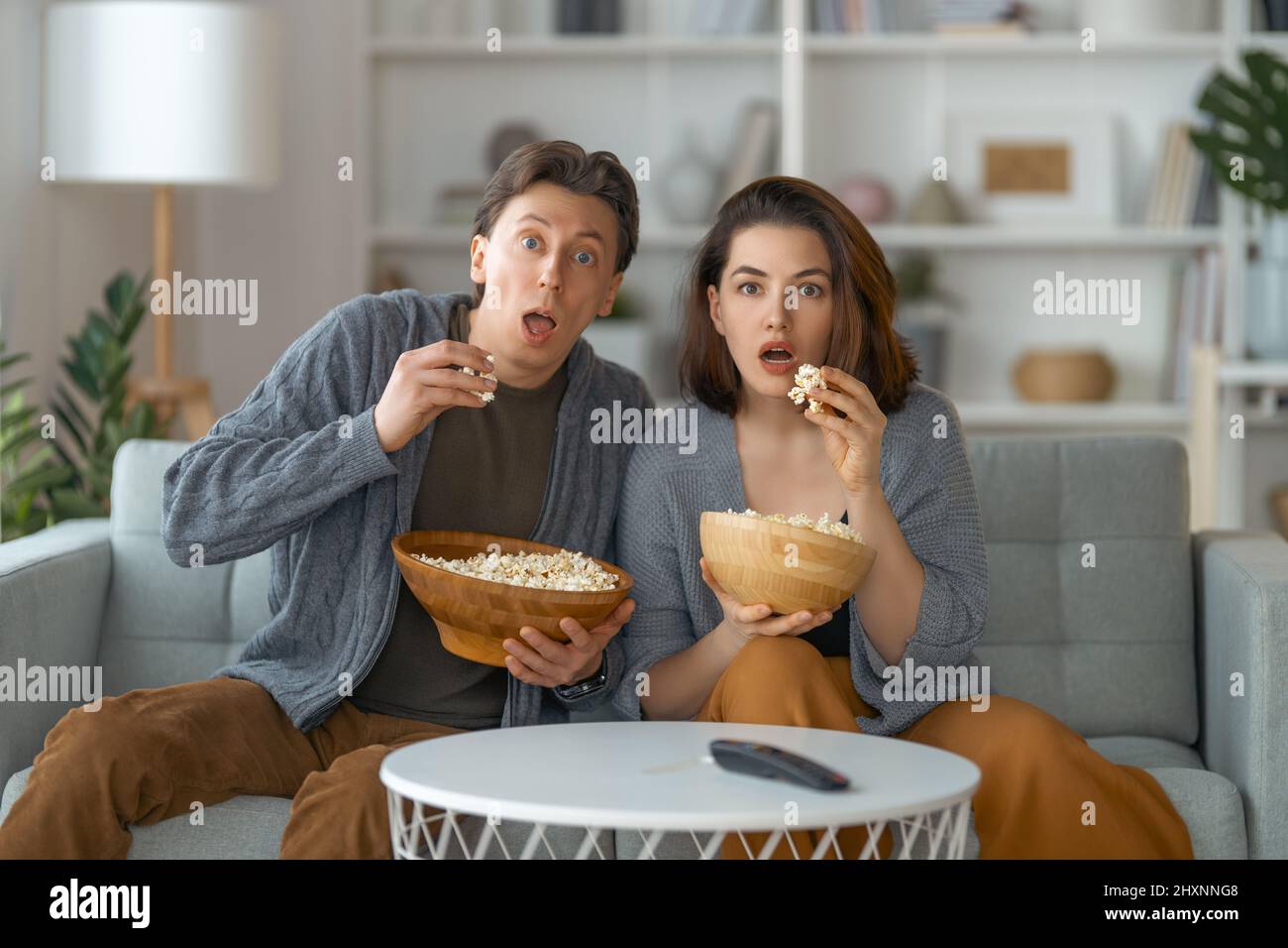 Shocked family with popcorn sitting on sofa and watching TV at home ...