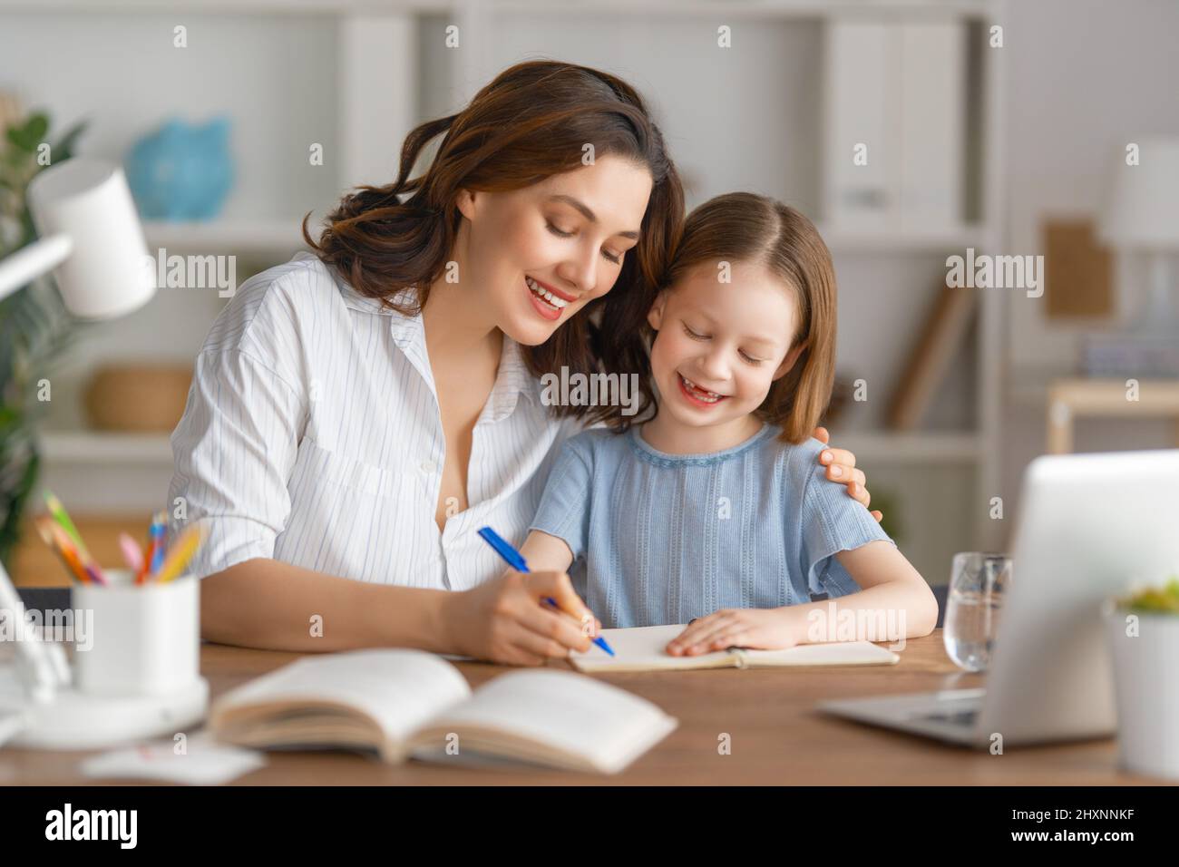Happy child and adult are sitting at desk. Girl doing homework or ...