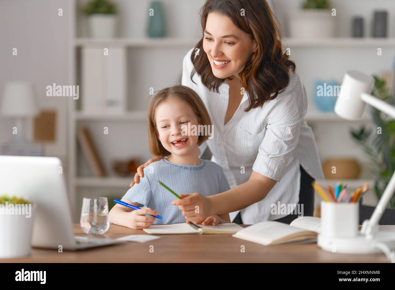 Happy child and adult are sitting at desk. Girl doing homework or ...