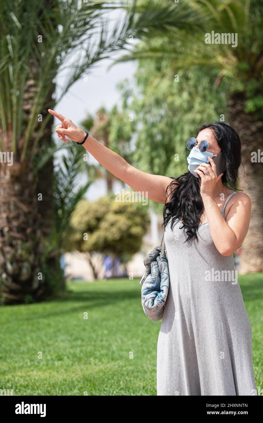 Mid age woman wearing surgical face mask talking on the phone and ...