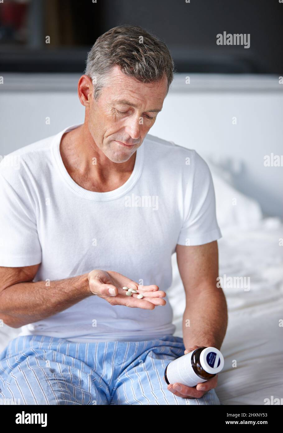 Taking his daily meds. Shot of a serious mature man sitting on a bed ...