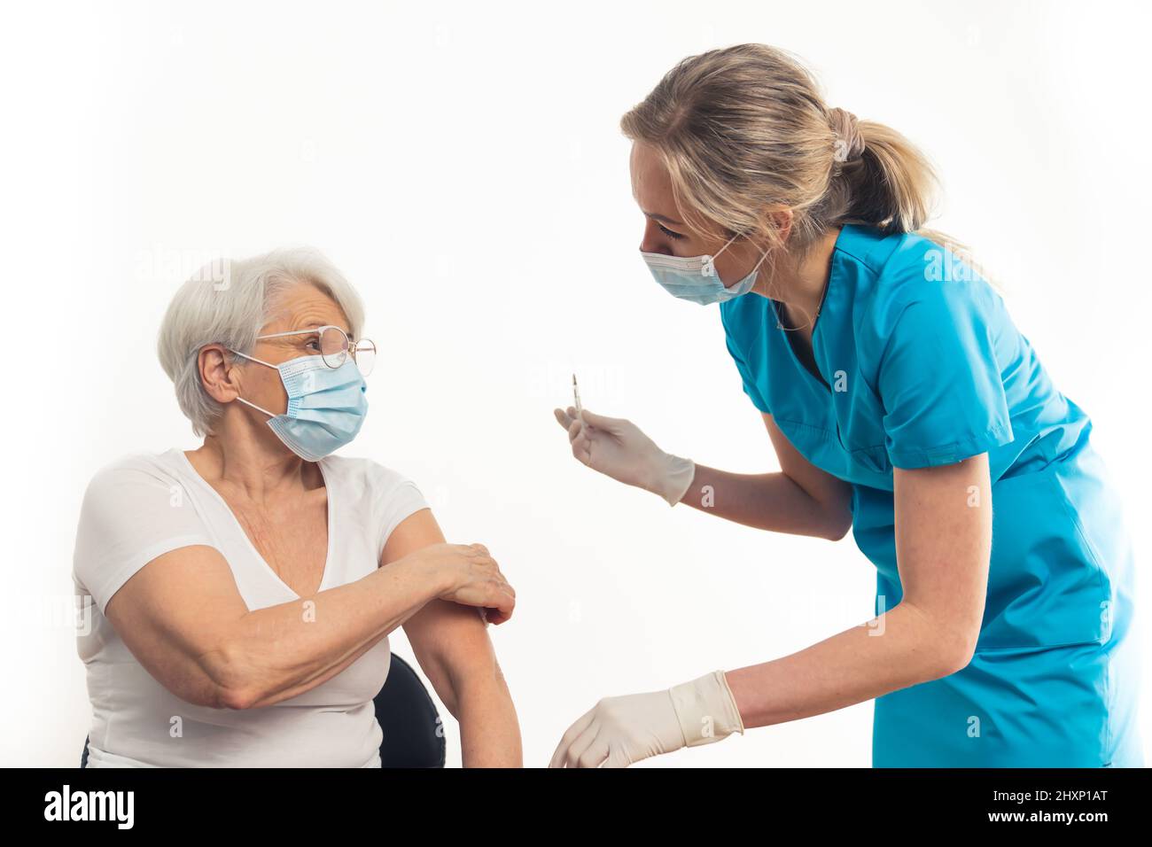 Masked caucasian nurse vaccinating elderly grey-haired woman ...