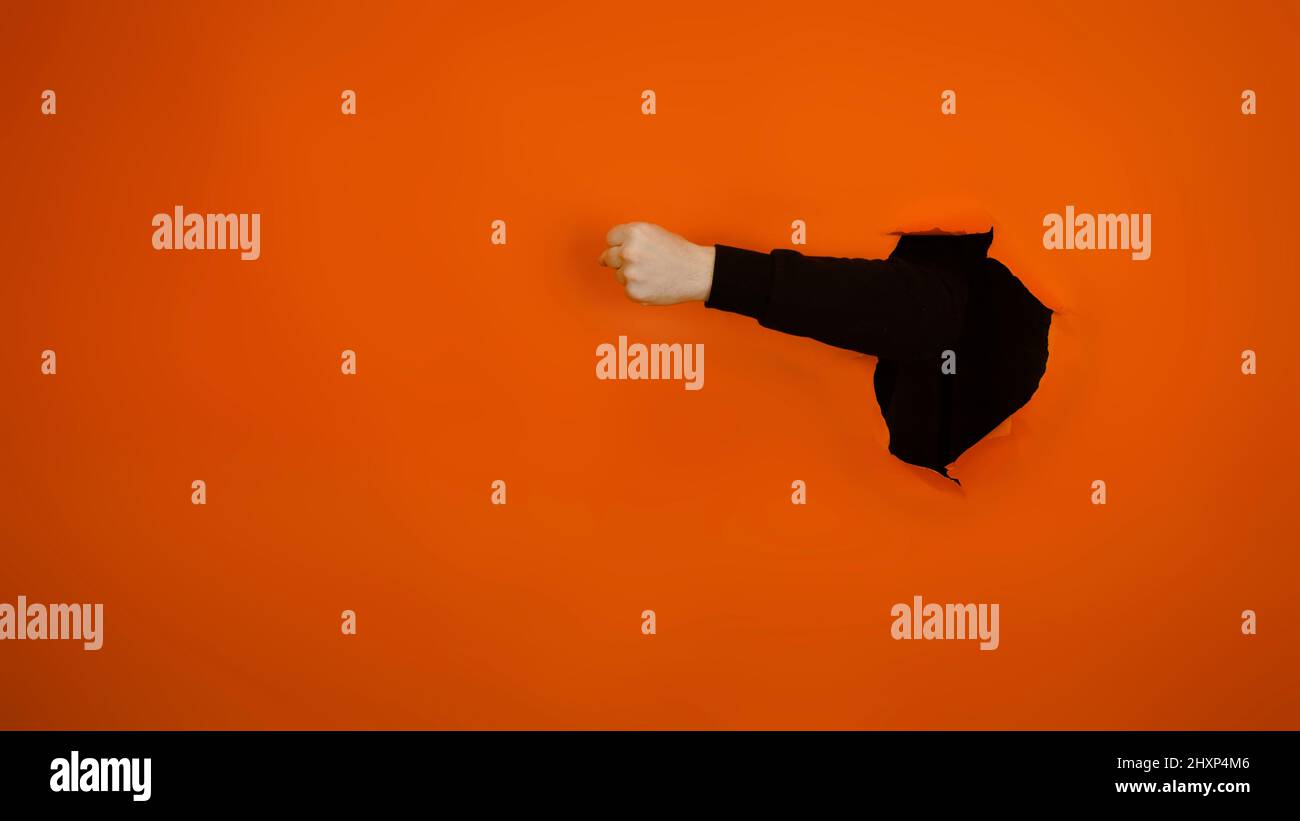Man's hand showing fist and sticking out of hole of orange background ...
