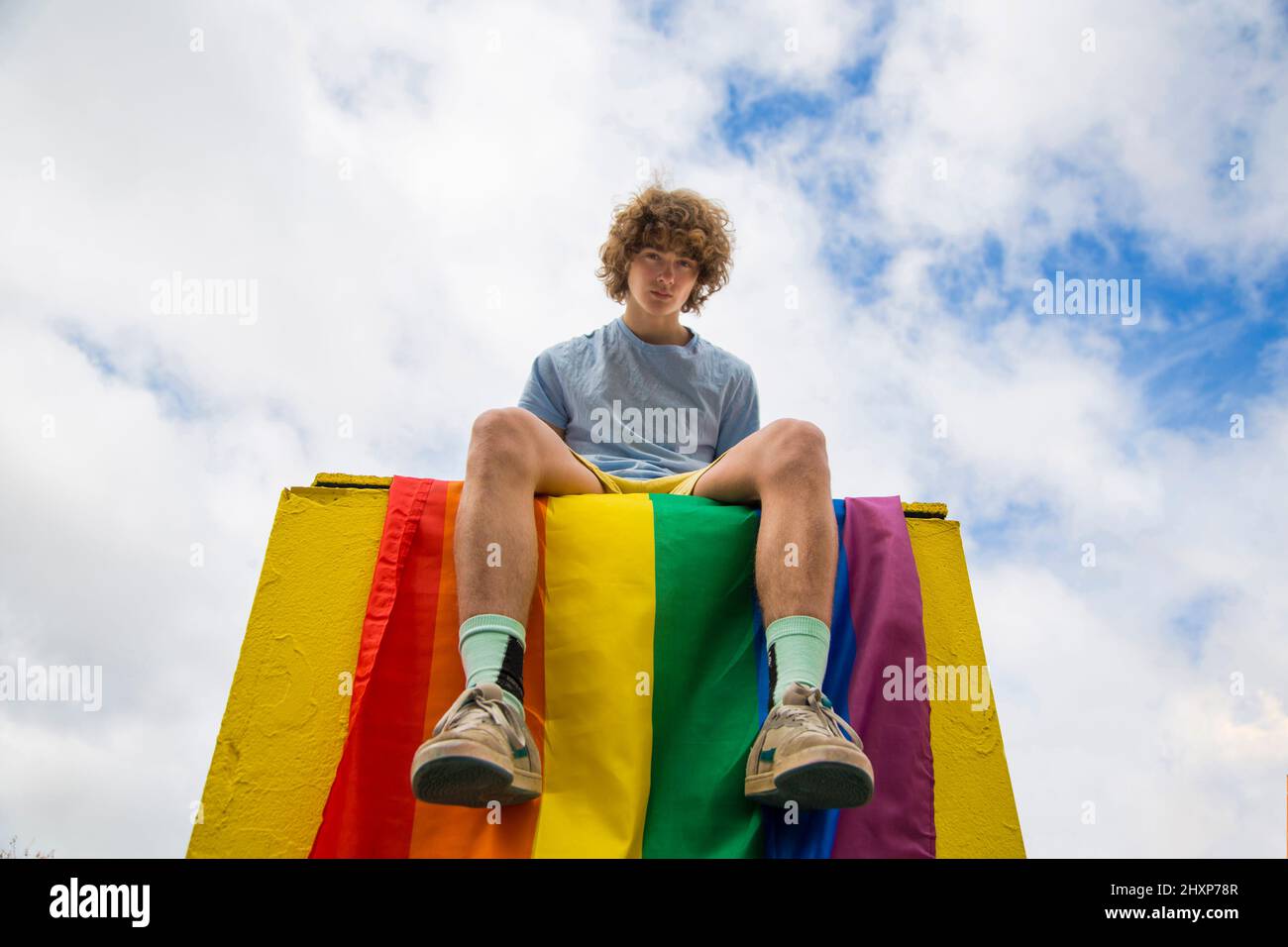 gay guy posing sitting on a gay pride flag with the sky in the ...