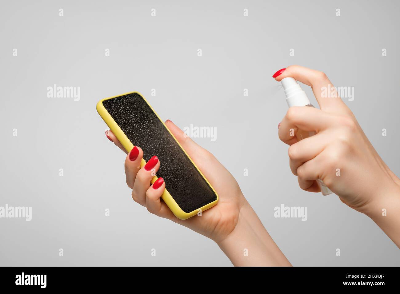 Woman's hands spray disinfectant on mobile phone to clean and protect ...