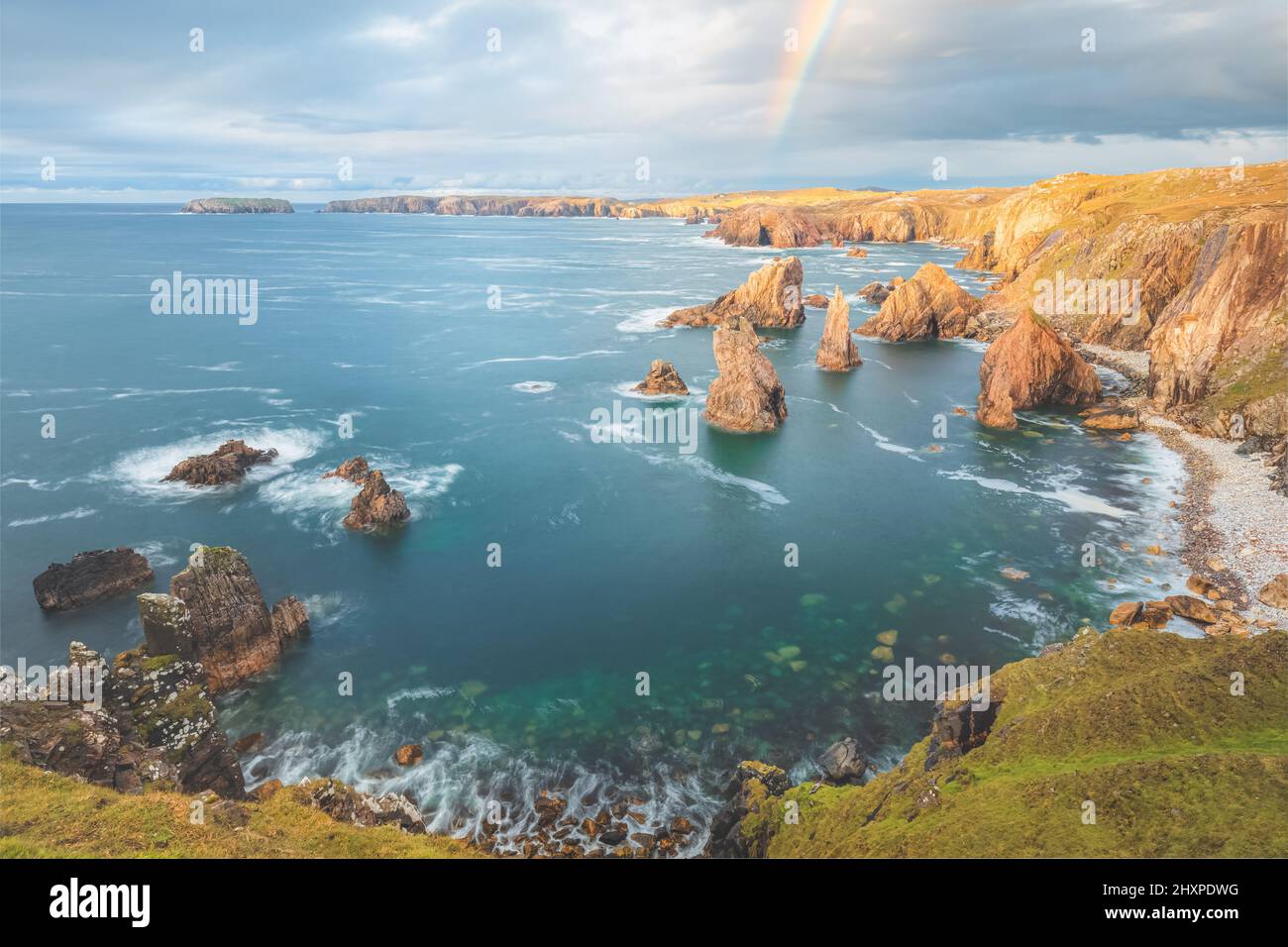 Golden hour light and rainbow over dramatic rocky landscape seascape of ...