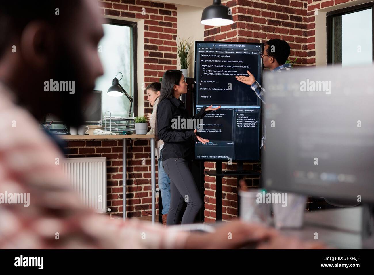 Software developers standing near vertical screen talking about ...