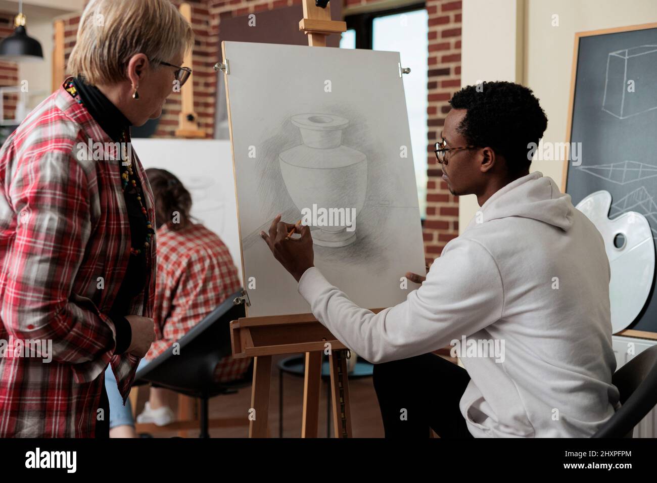 Senior painter teacher explaining illustration technique to young ...