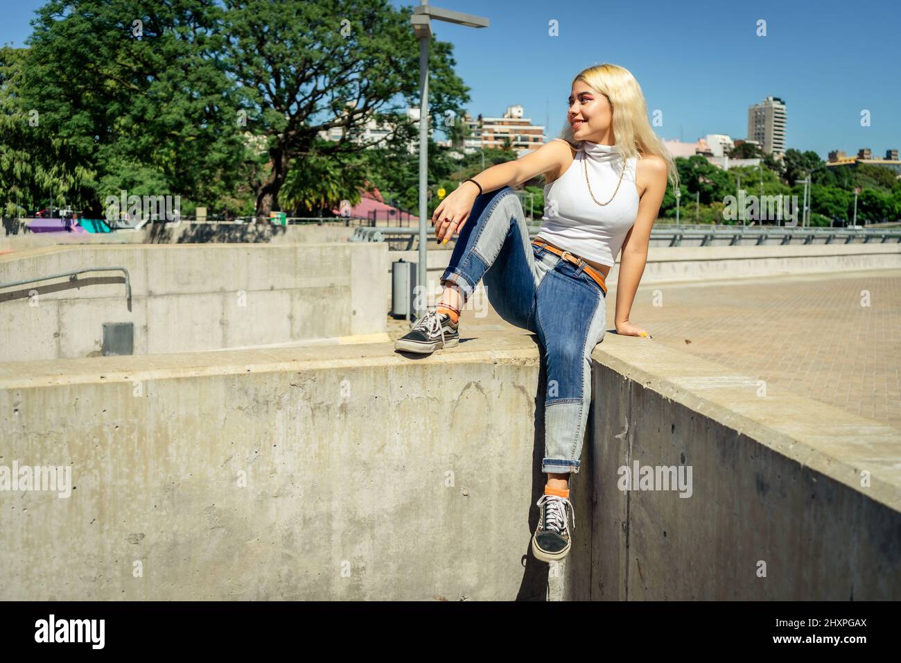 A Beautiful young latin woman sitting smiling on a cement railing with ...