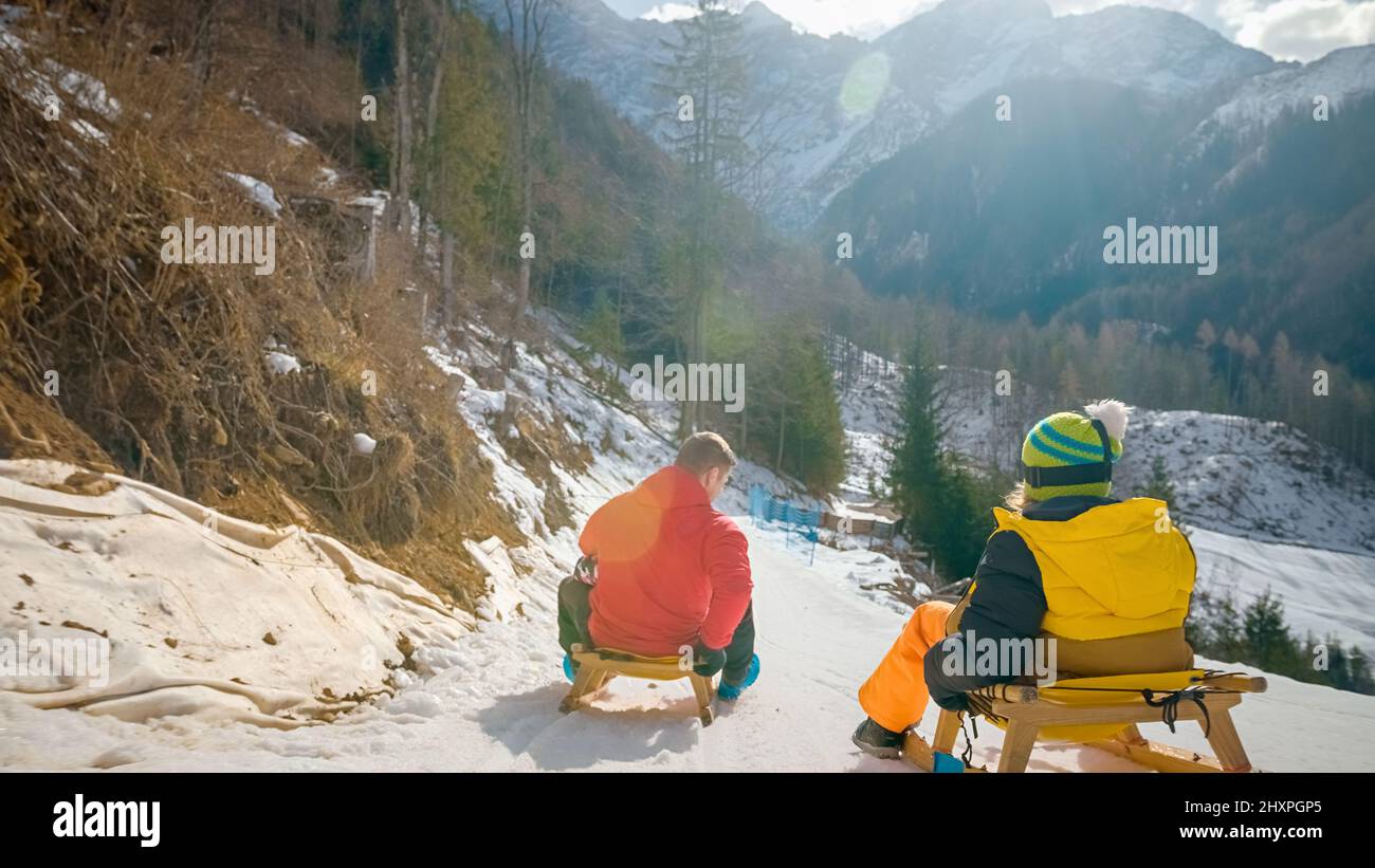 Father and son, sledding on wooden sleds from the top of the snowy ...