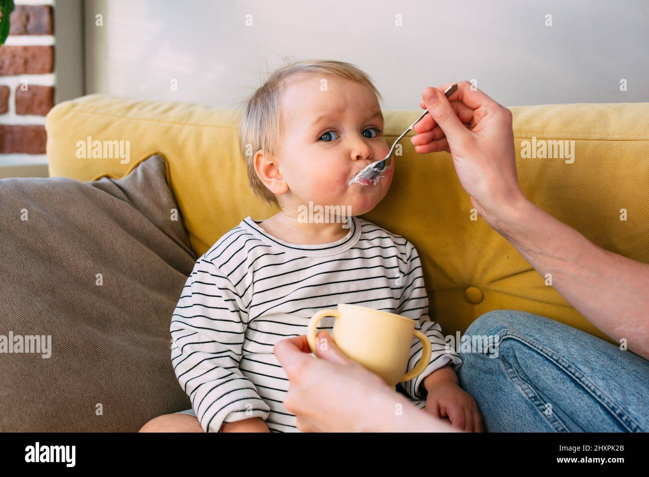 Mom feeds a small child at home with yogurt from a spoon. Family ...