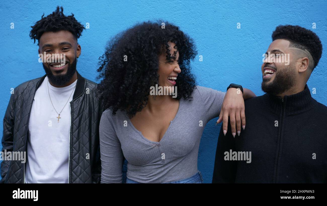 Three latin friends laughing and smiling leaning on blue wall ...