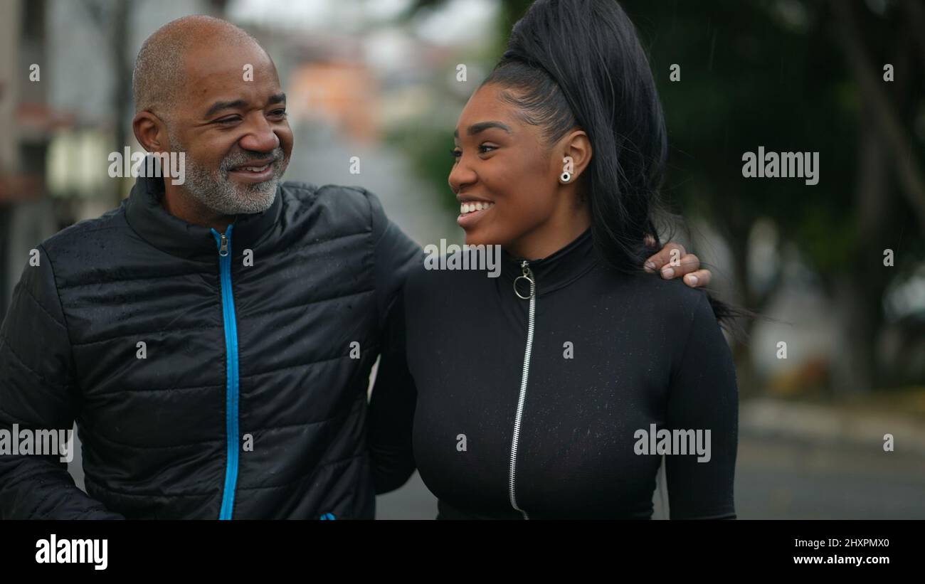 A black father and teen daughter walking together outside in street ...