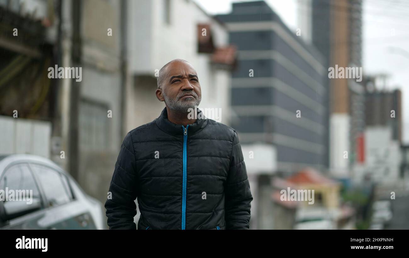 A senior black man standing outside in the rain looking at sky drizzle ...