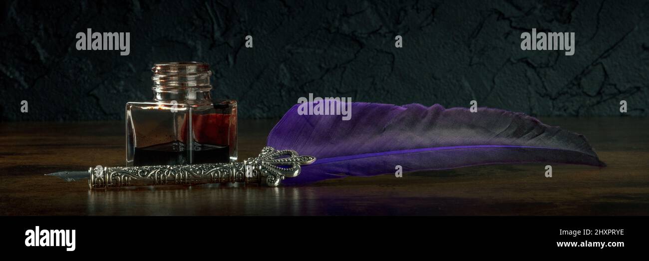 A quill pen with a vintage ink well on a black background, panoramic ...