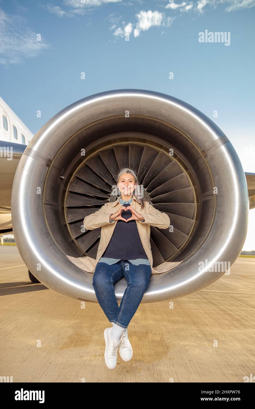 Cheerful woman sitting in aircraft engine and doing heart sign Stock ...
