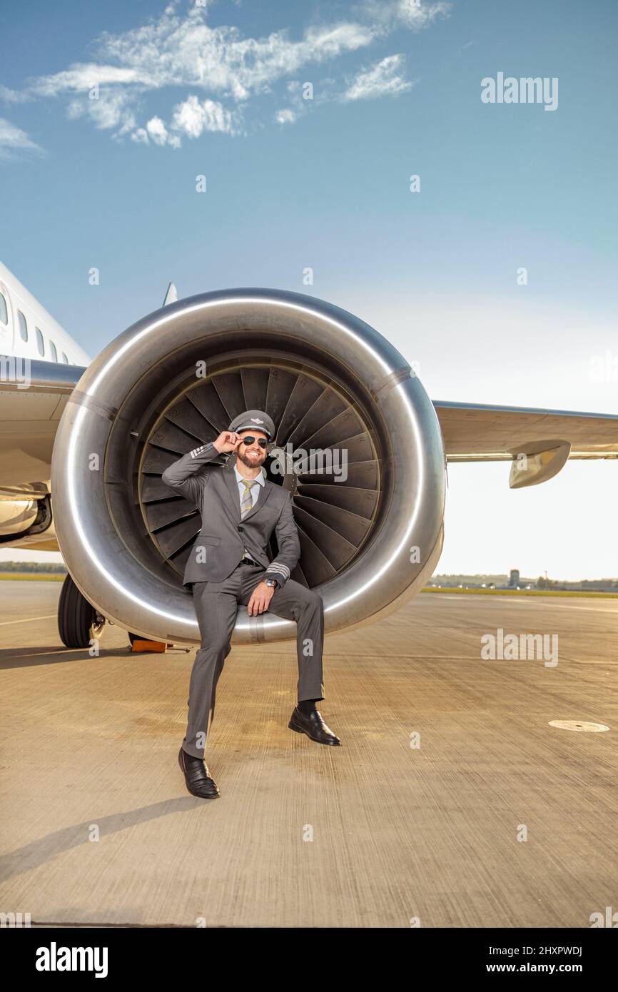 Joyful aircraft pilot sitting in airplane engine at airport Stock Photo ...