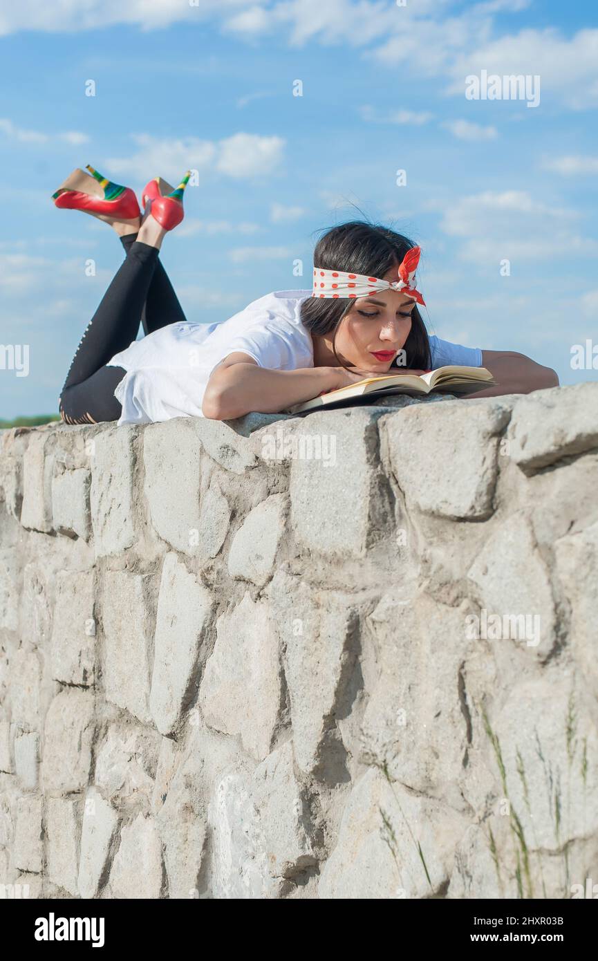 Beautiful girl lying on wall and enjoying a book reading. Close up ...