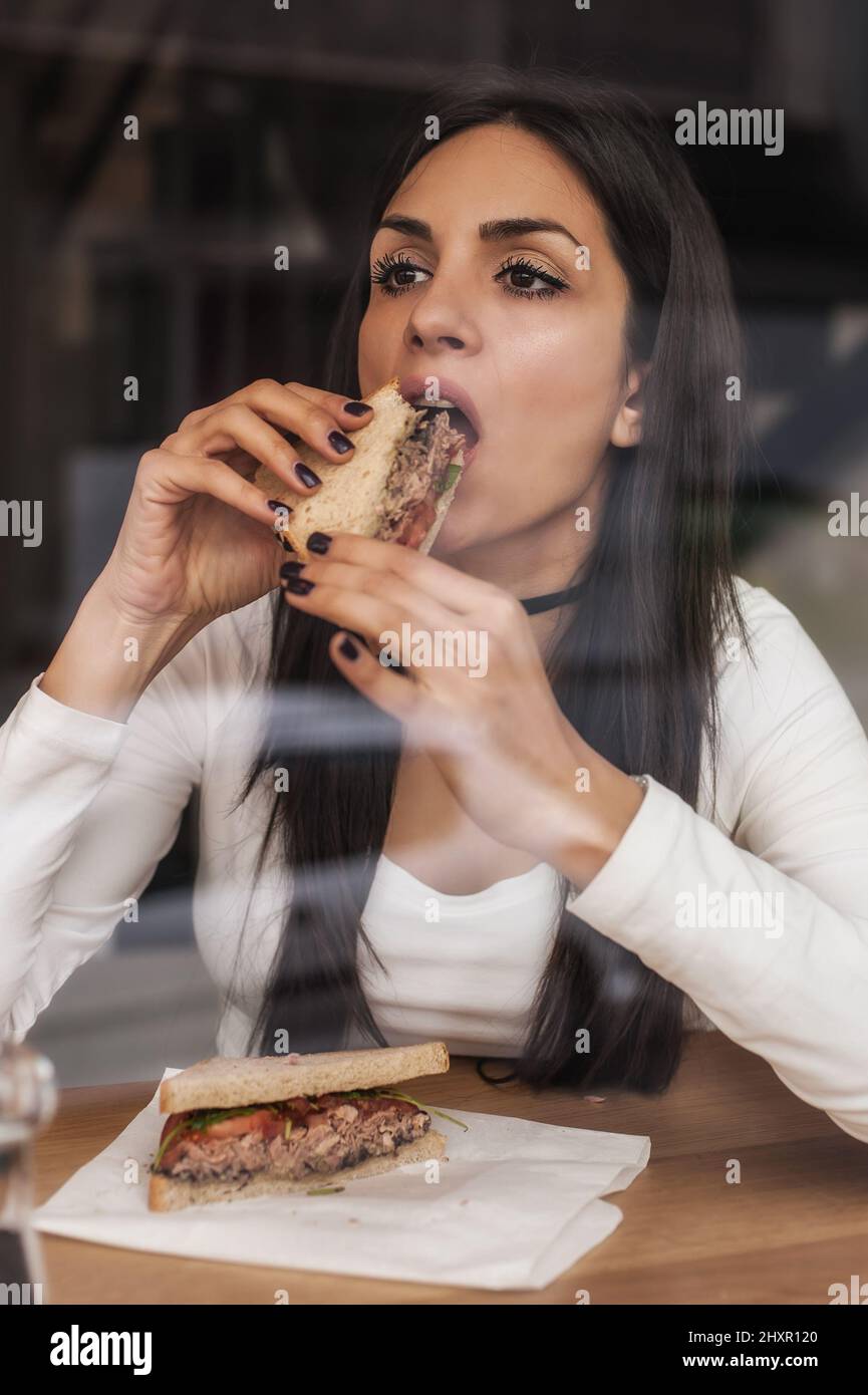 Portrait of young woman eating a sandwich in fast food cafe. Cafe ...