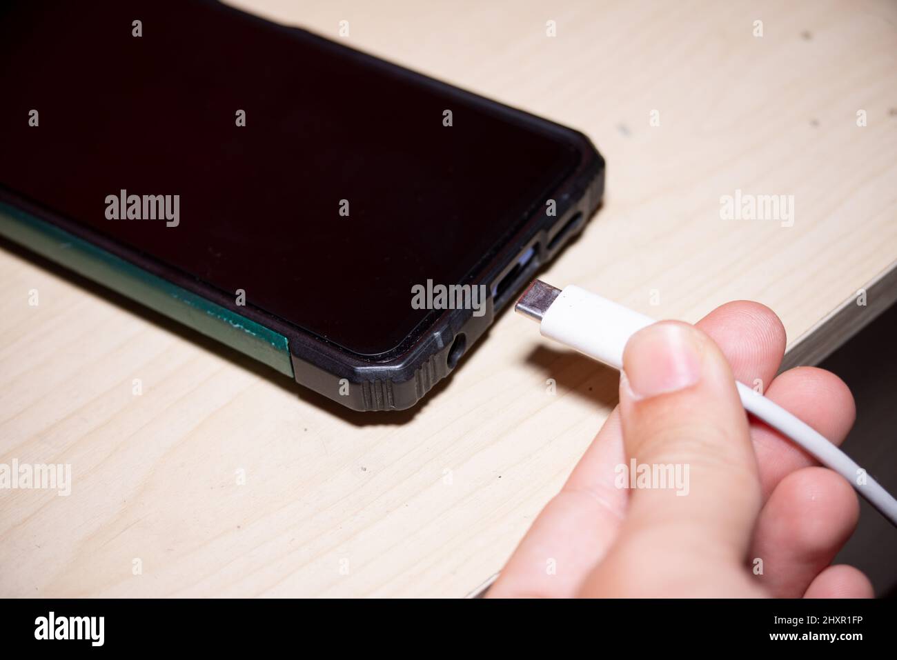 Hand Mobile smart phones charging on wooden desk Stock Photo - Alamy