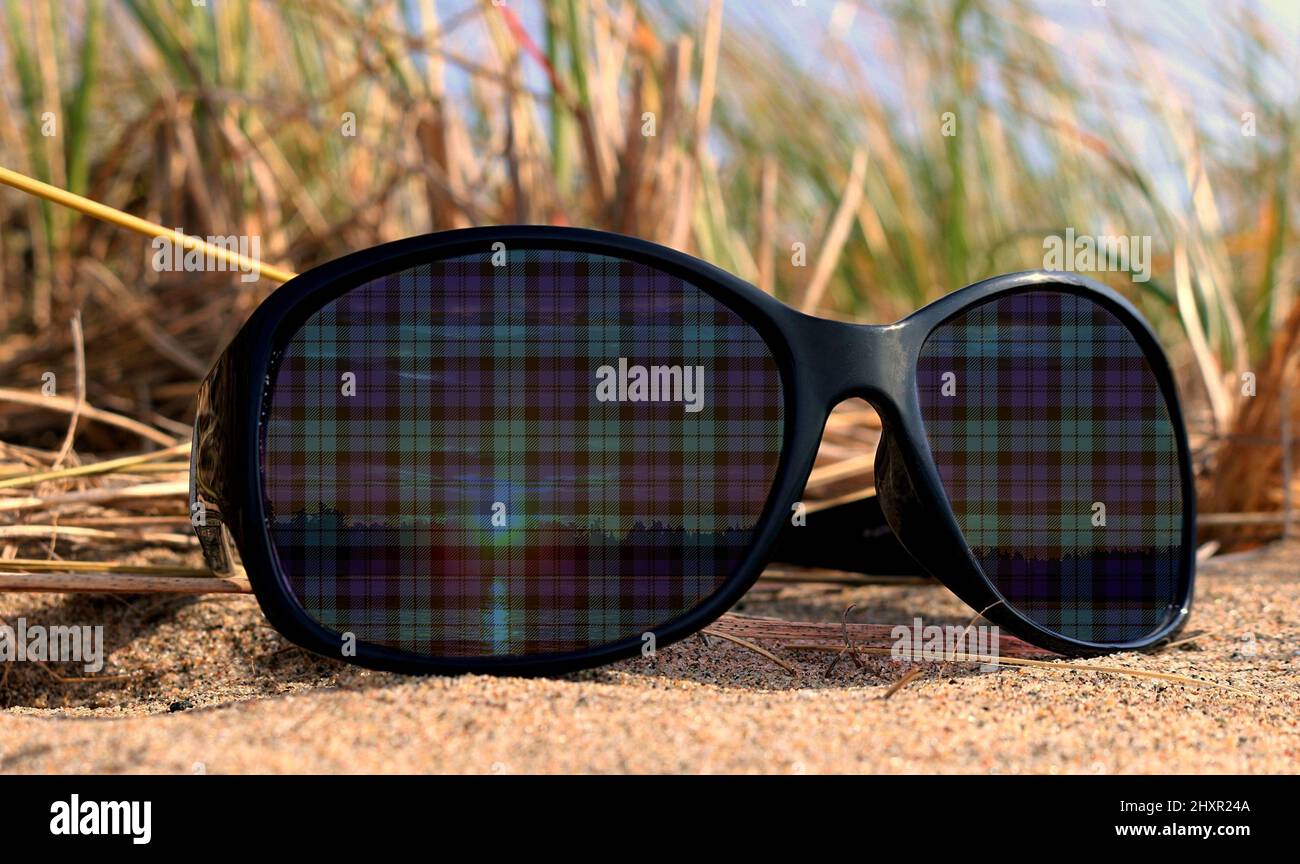 Gaelic tartan on sunglasses on the beach with grass and water behind ...