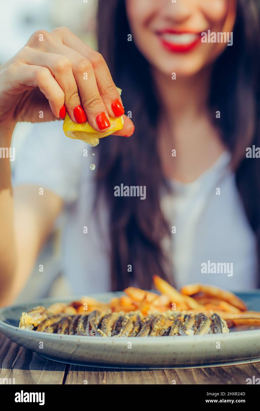 Young woman squeeze lemon on a portion of fish in a restaurant, having ...