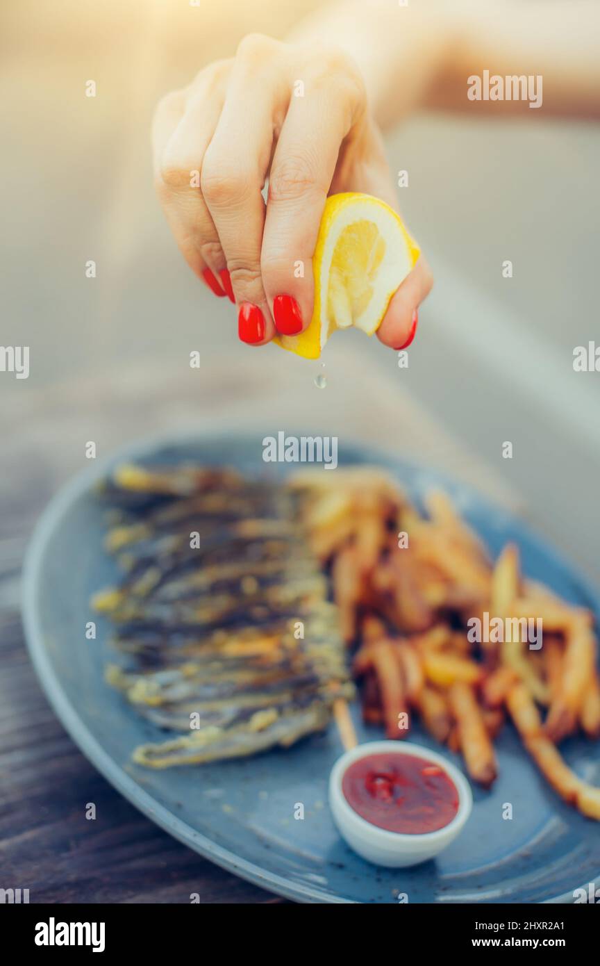 Young woman squeeze lemon on a portion of fish in a restaurant, having ...