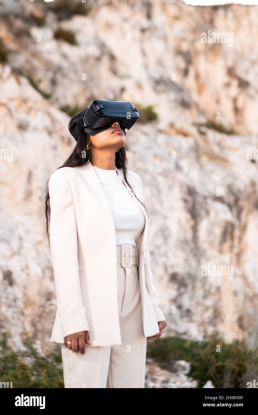 Elegant woman dressed in a white suit using a virtual reality goggles ...