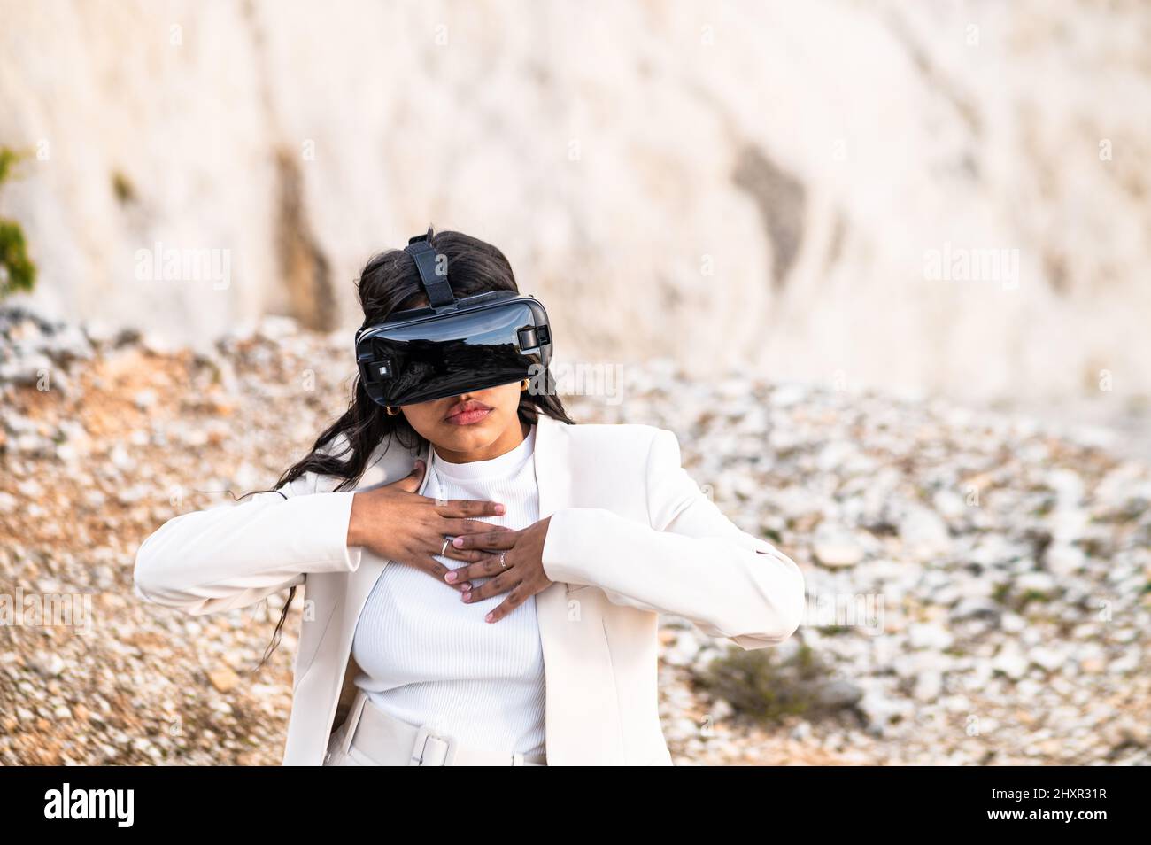 Elegant woman dressed in a white suit using a virtual reality goggles ...