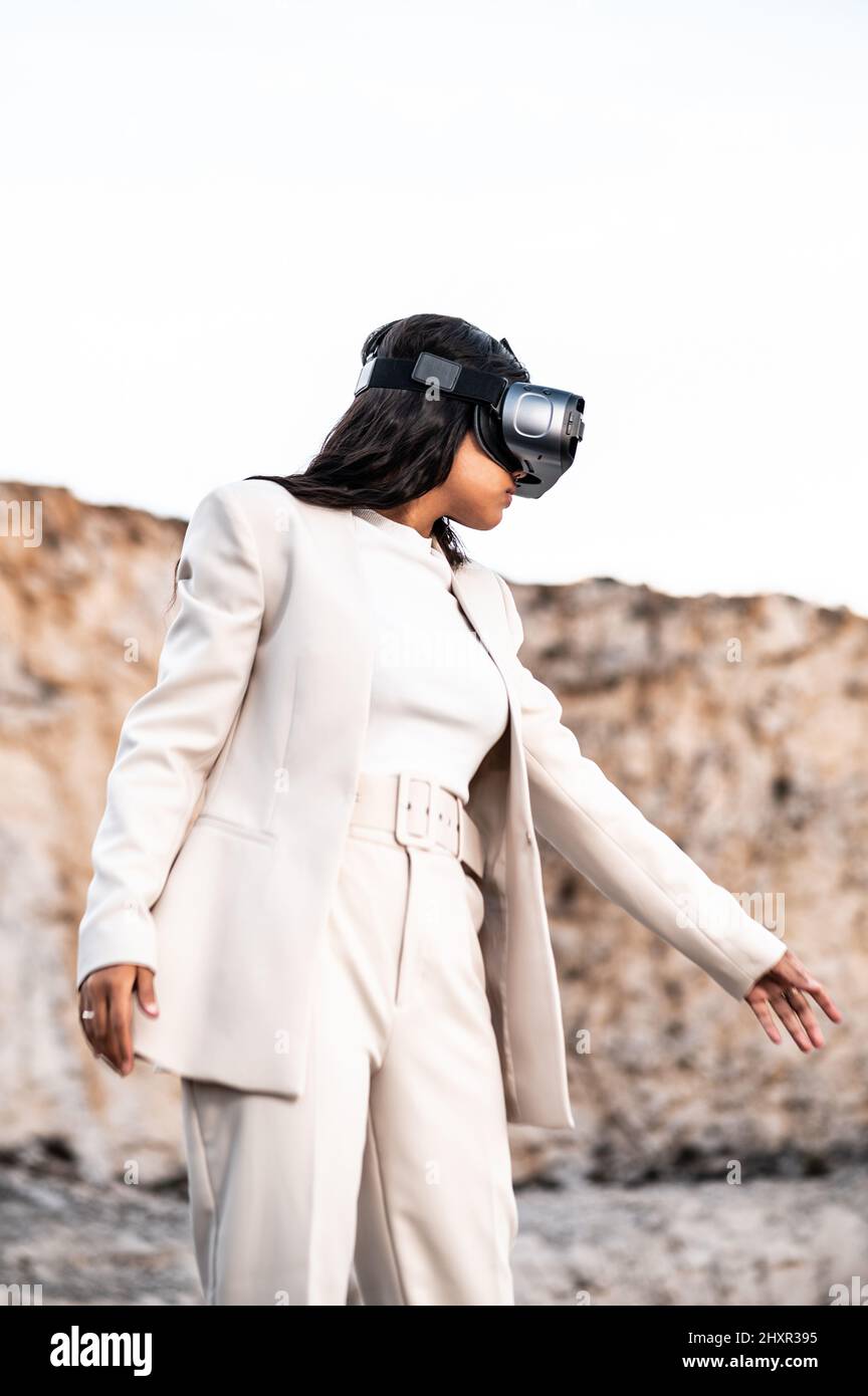 Elegant woman dressed in a white suit using a virtual reality goggles ...
