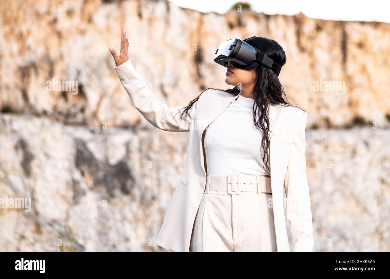 Elegant woman dressed in a white suit using a virtual reality goggles ...