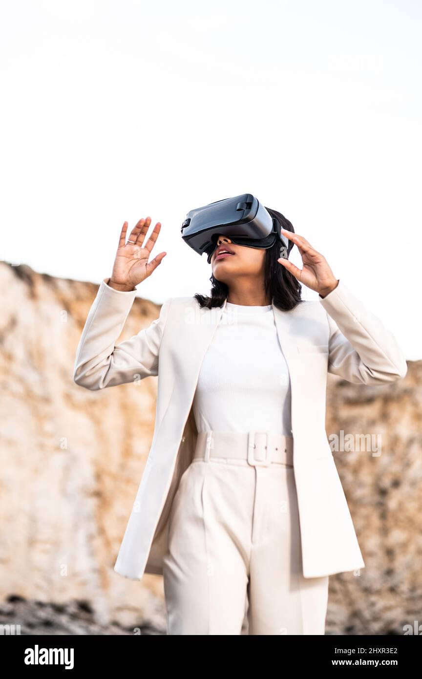 Elegant woman dressed in a white suit using a virtual reality goggles ...