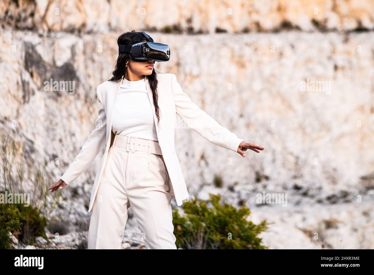 Elegant woman dressed in a white suit using a virtual reality goggles ...
