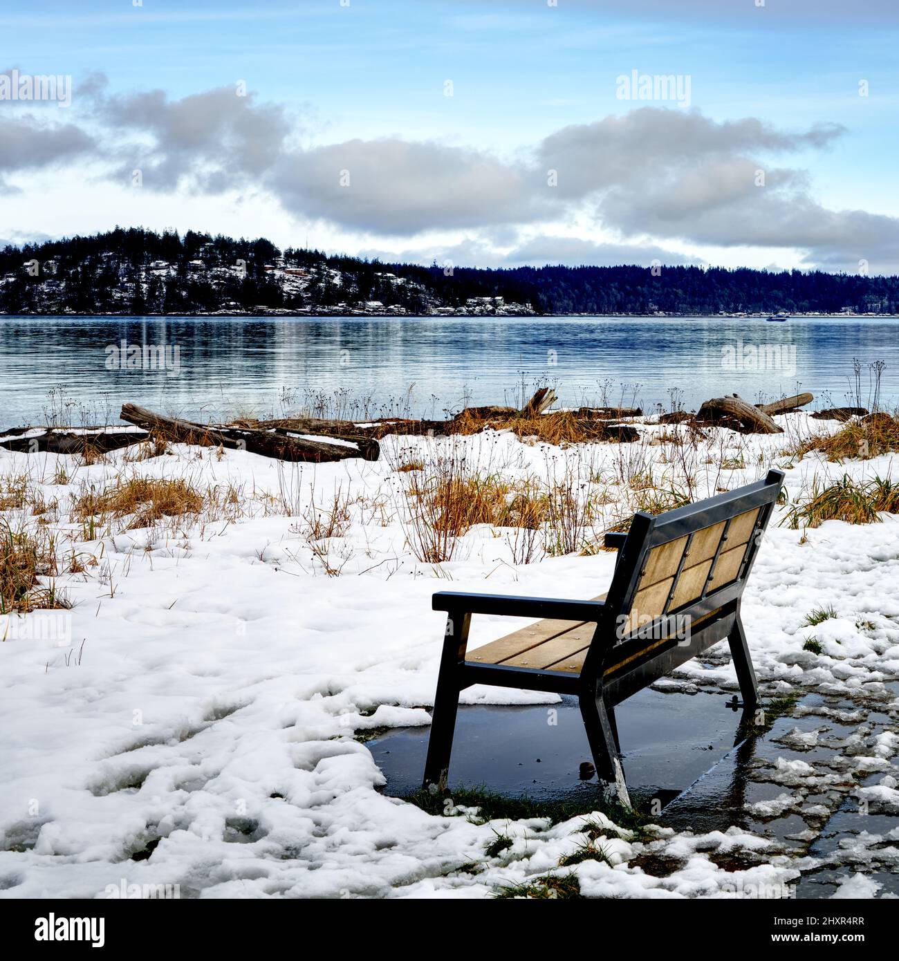 An empty park bench on a winter day with a view over the ocean of a ...