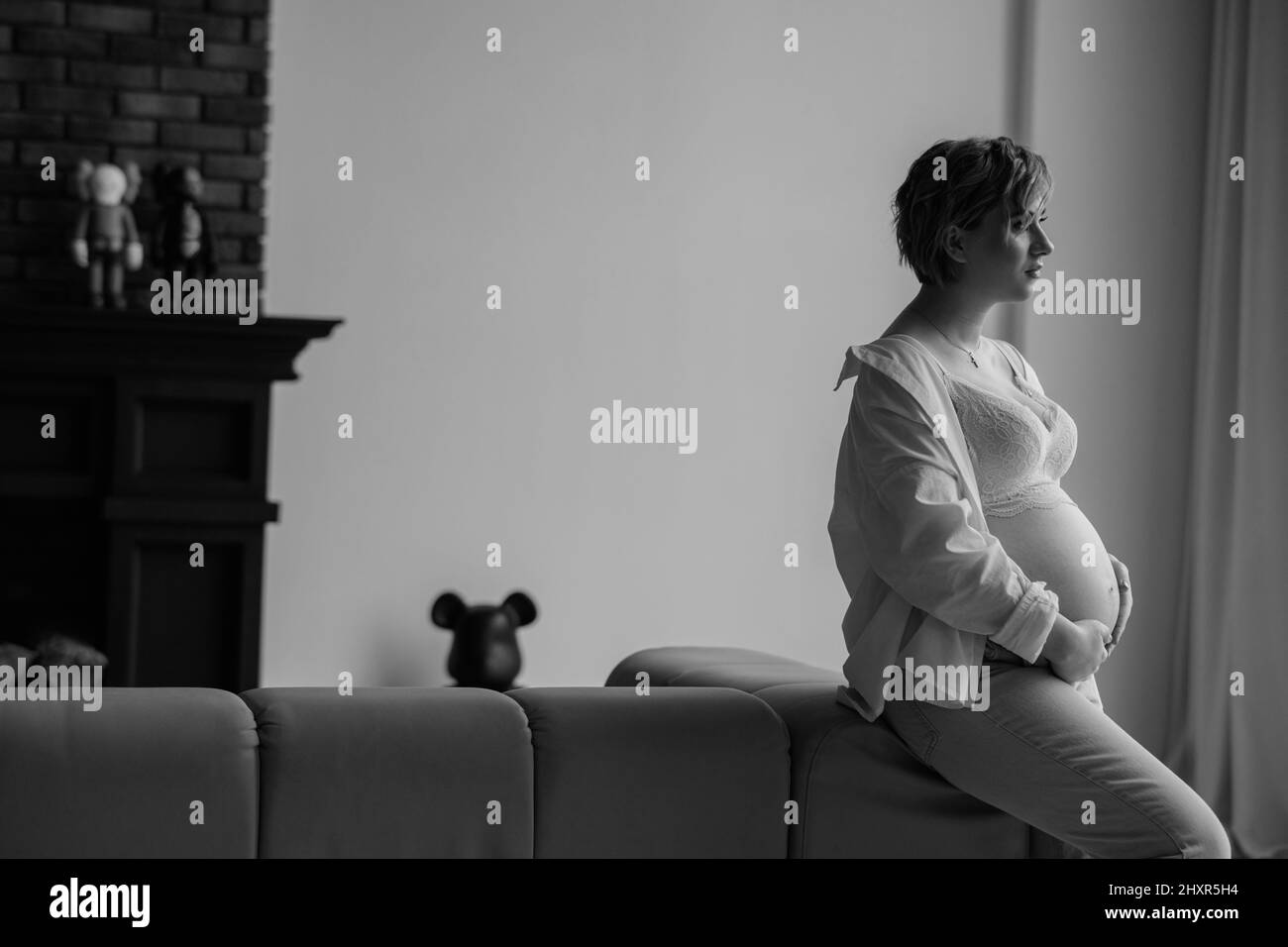 Young happy pregnant woman sitting on the edge of sofa in room ...