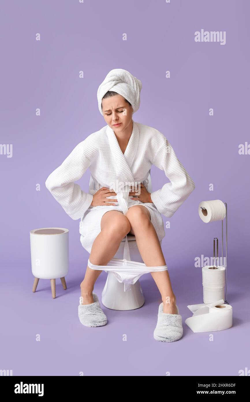 Young woman suffering from diarrhea while sitting on toilet bowl ...