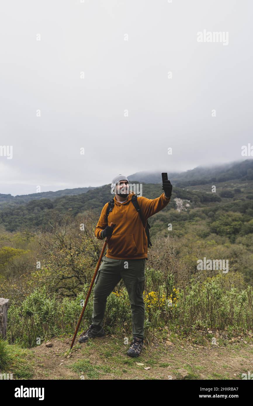 Vertical shot of the Caucasian male hiking in the forest and taking ...