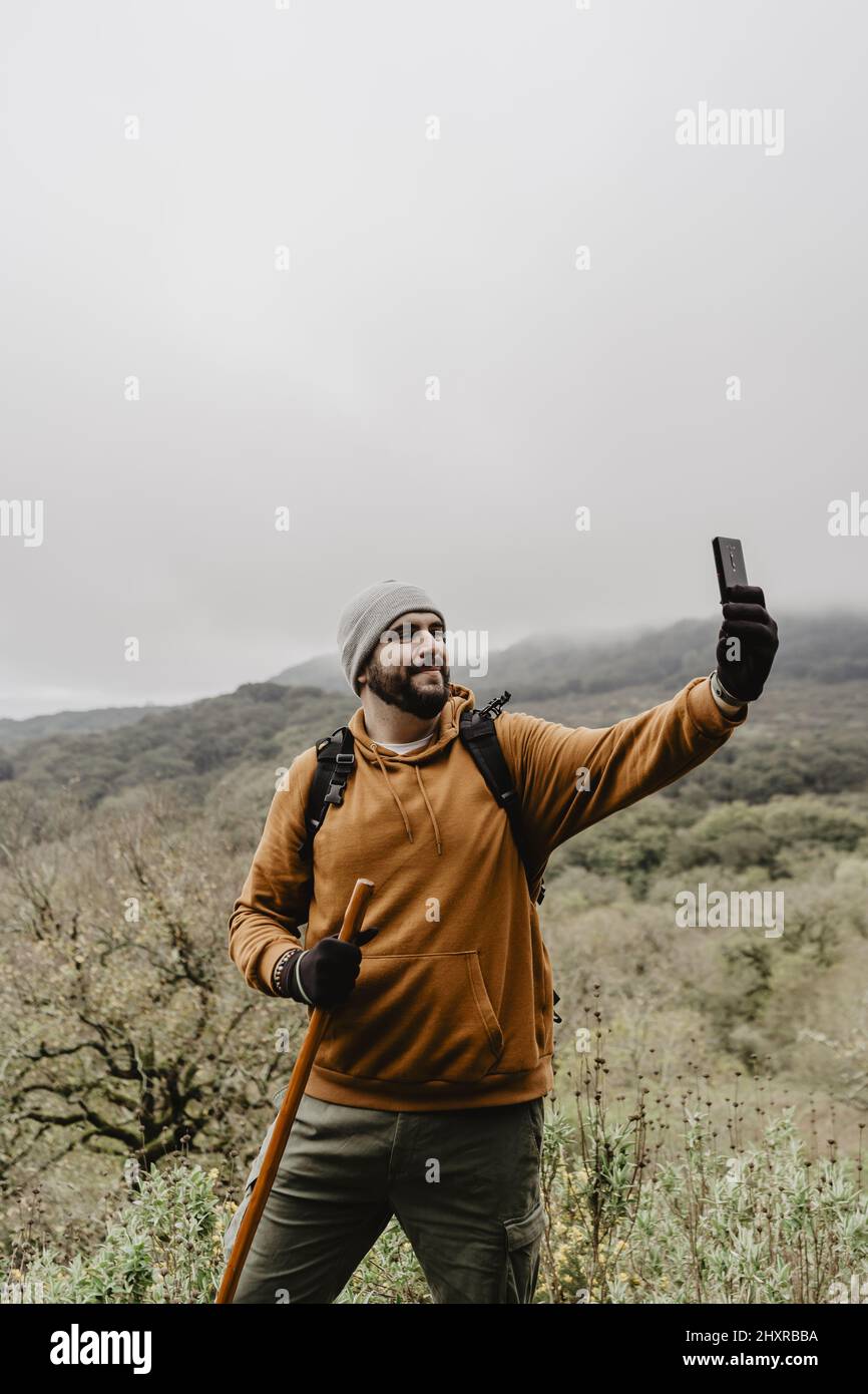 Vertical shot of the Caucasian male hiking in the forest and taking ...