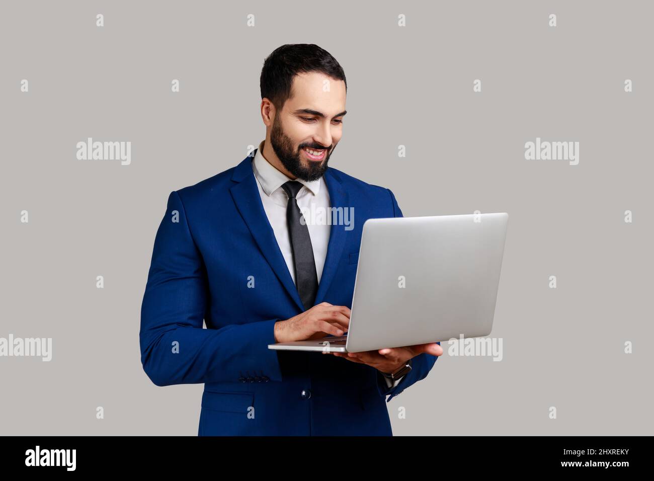 Smiling bearded man holding laptop, typing on keyboard, surfing ...