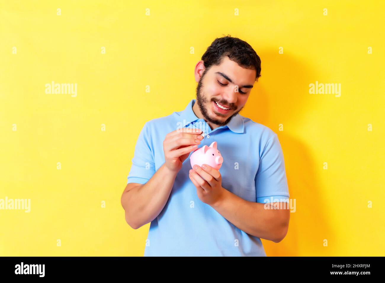 Man putting money in a piggy bank isolated on yellow background Stock ...