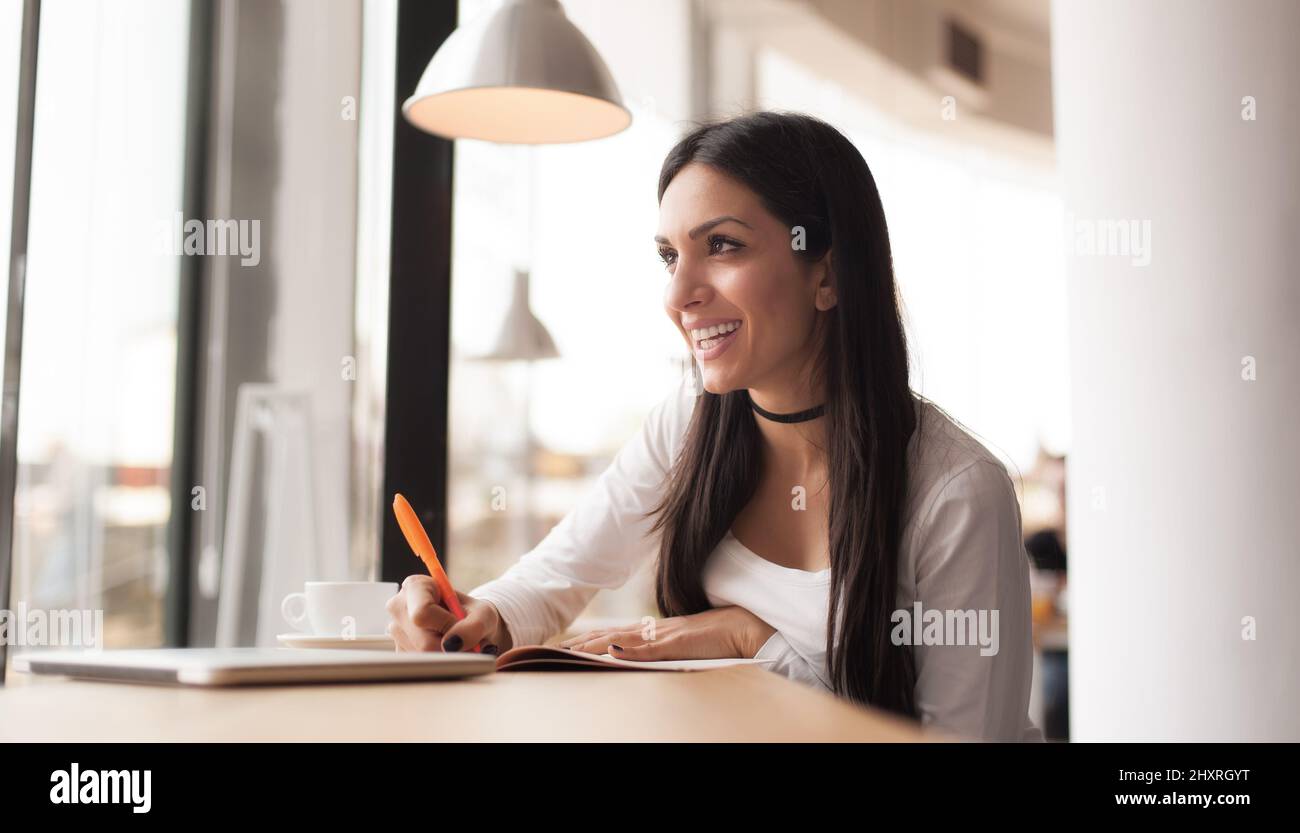 Attractive young woman writing in her notebook and drinking coffee in ...