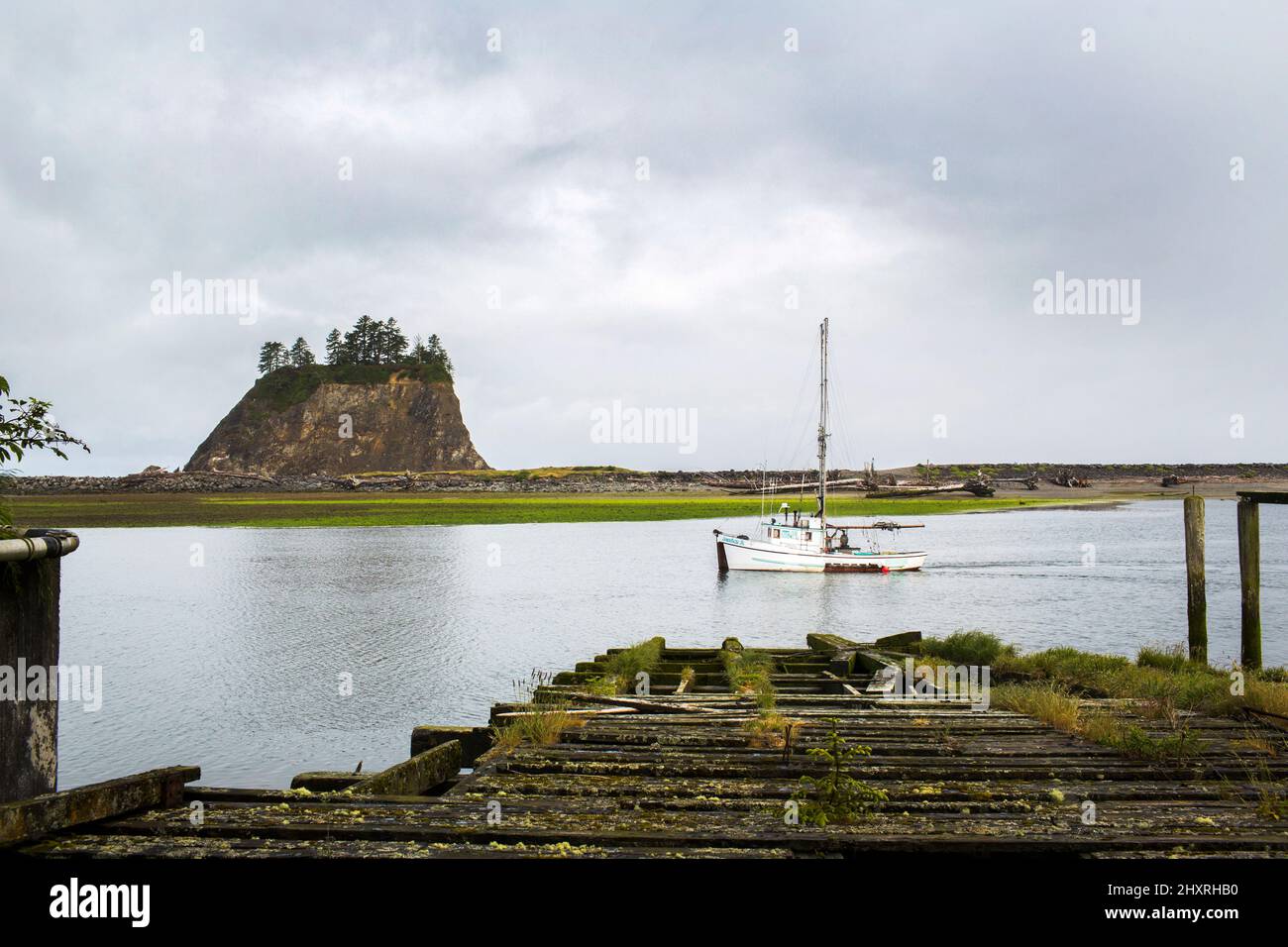 A fishing boat motors on calm water with wild rocky island, old dock ...