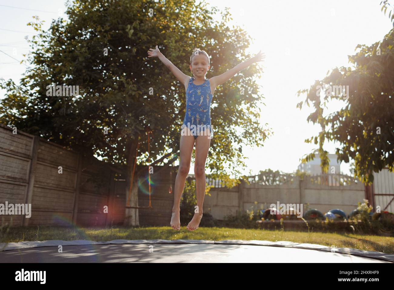 little sports girl jumps on a trampoline. Outdoor shot of girl jumping ...