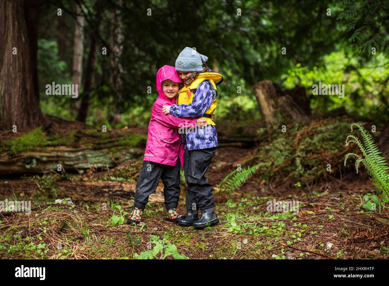 Two young girls in rain gear stand and hug in a forest Stock Photo - Alamy